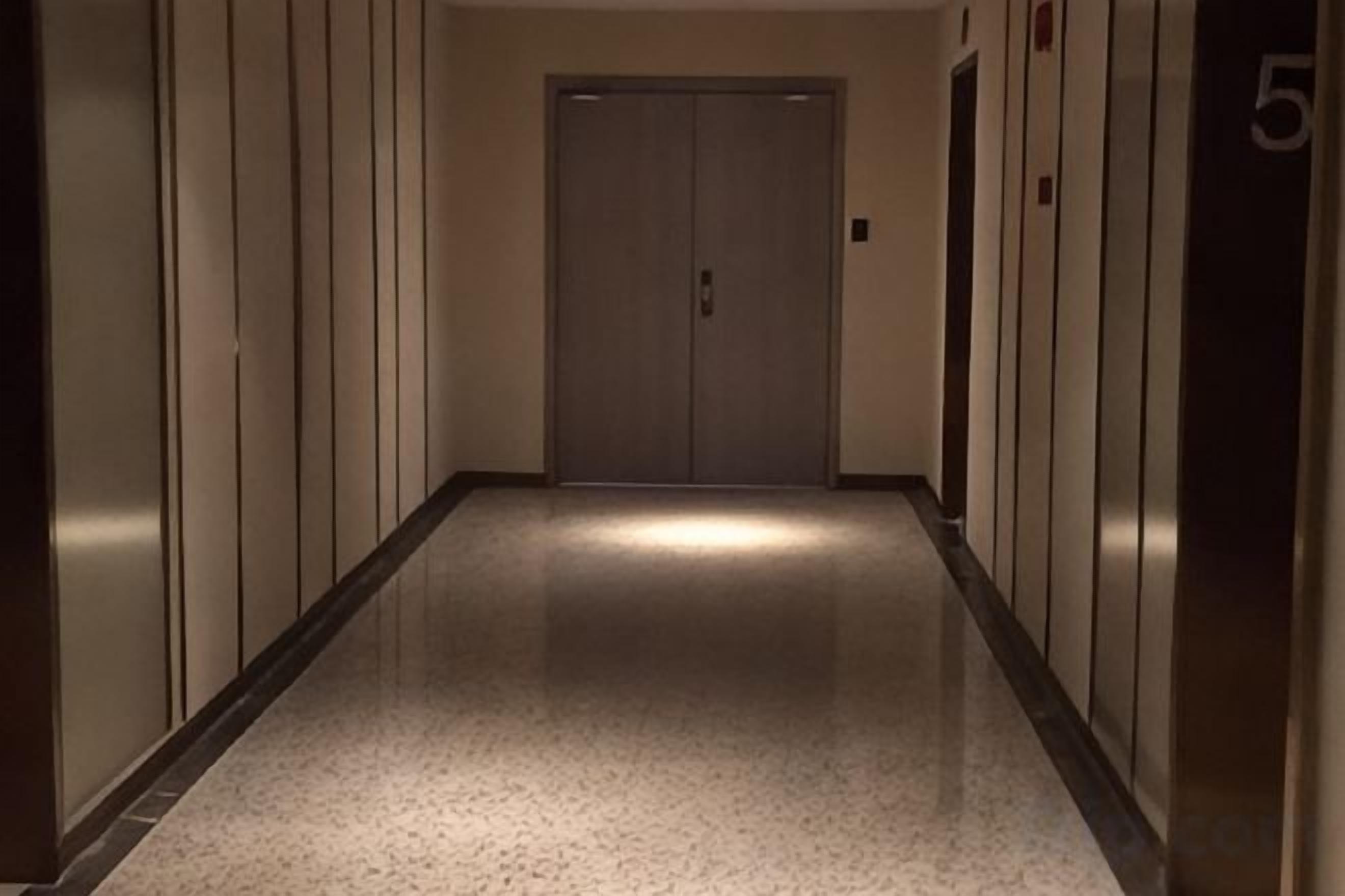 Corredor com porta no fim, ladeado por paredes com linhas verticais e piso refletivo.