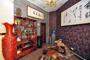 Um quarto com decoração em estilo tradicional chinês, incluindo um vaso vermelho, um armário de madeira com objetos decorativos e uma grande pintura de caligrafia na parede.