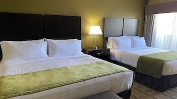 Quarto de hotel com duas camas, uma mesa de cabeceira com abajur e uma janela com cortinas.
