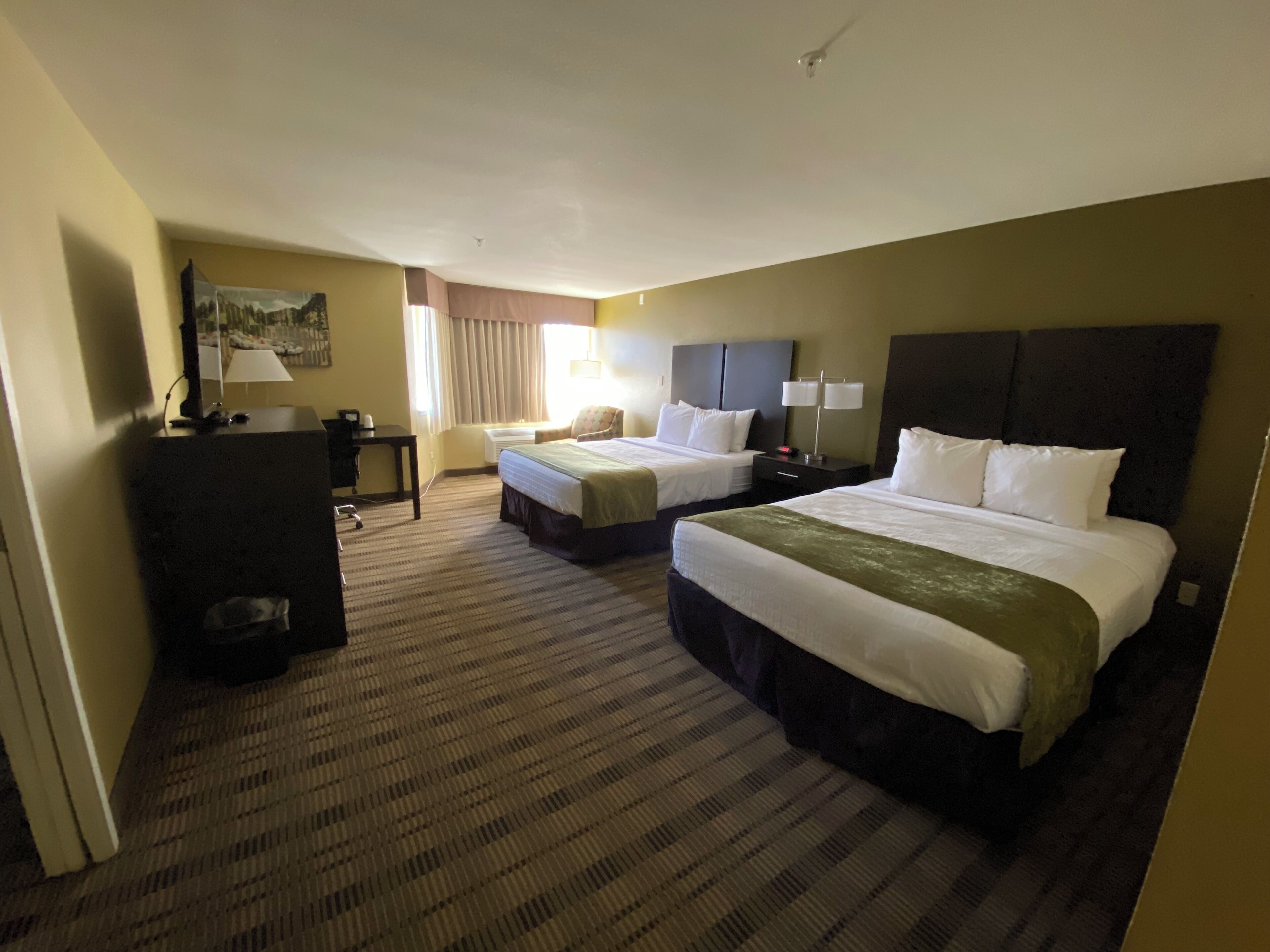Quarto de hotel com duas camas, uma escrivaninha, uma cadeira e uma janela com cortinas.
