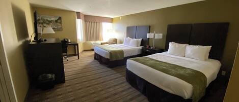 Quarto de hotel com duas camas, uma escrivaninha, uma cadeira e uma janela com cortinas.