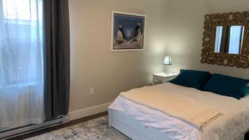 Quarto com cama, mesa de cabeceira, abajur, quadro e espelho decorativo.