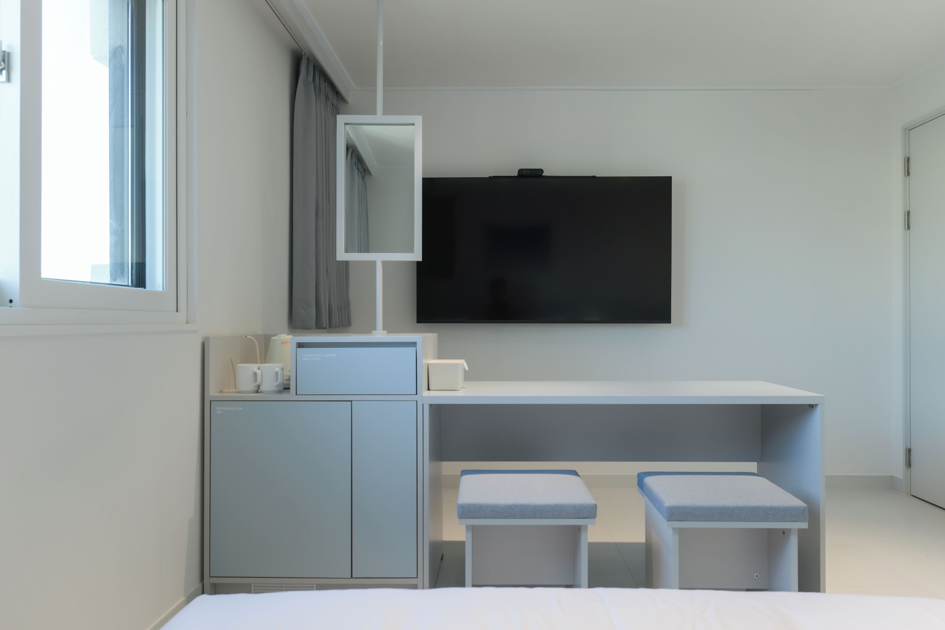 Quarto de hotel moderno com cama, escrivaninha, televisão e minibar.