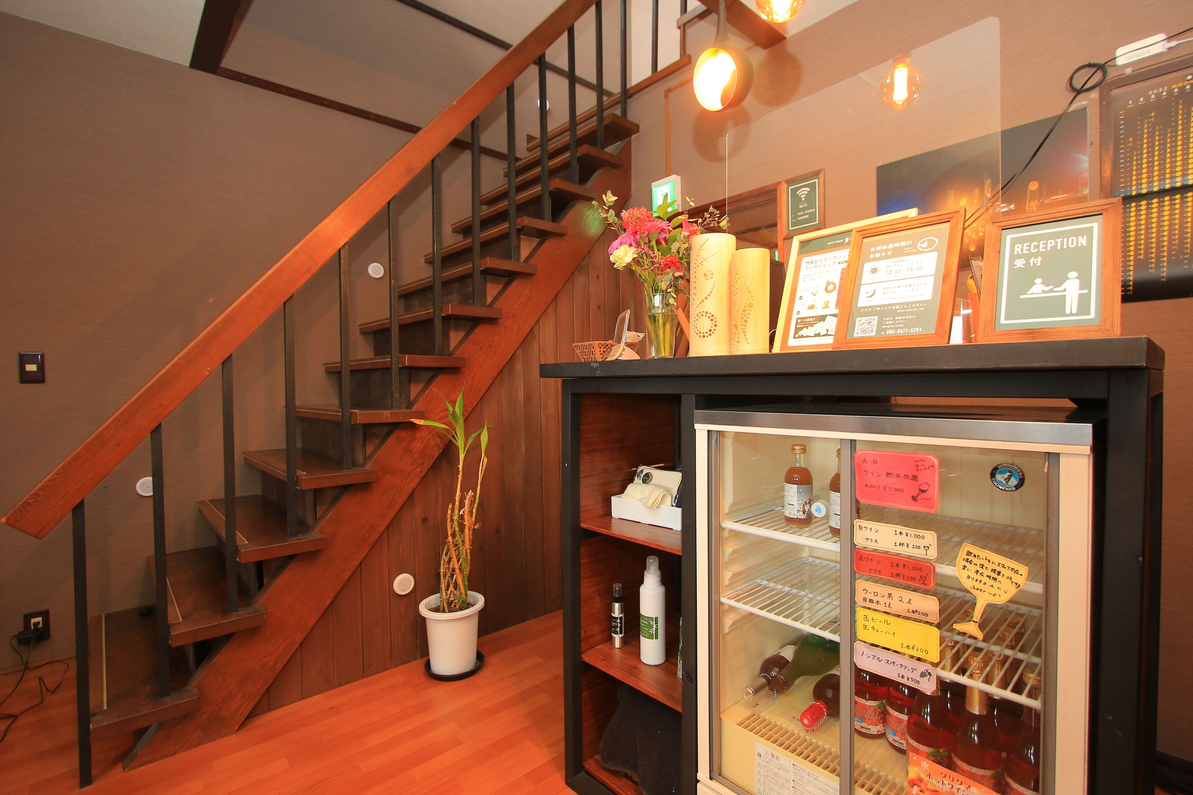 Uma área de recepção com escada de madeira, planta em vaso, vitrine de vidro com diversos objetos e placas informativas.