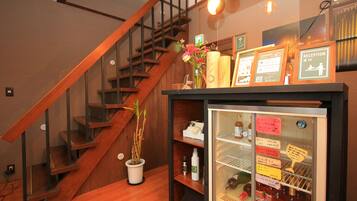 Uma área de recepção com escada de madeira, planta em vaso, vitrine de vidro com diversos objetos e placas informativas.