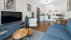 Uma sala de estar moderna com uma televisão de tela plana, um sofá azul, uma cadeira branca e uma mesa de centro de madeira.