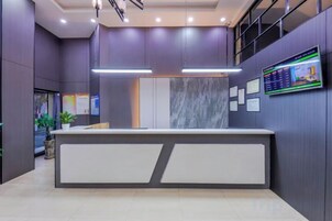 Uma área de recepção com balcão, um visor digital e um quadro de informações fixado na parede.