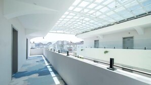 Um corredor de hotel moderno com teto de vidro, chão com padrão azul e vista para a paisagem urbana.