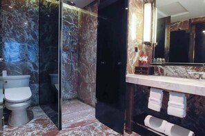 Um banheiro com piso de mármore, box de vidro, vaso sanitário e toucador com toalhas.