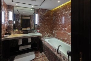 Uma casa de banho moderna com lavatório de mármore, um espelho grande e uma banheira independente.