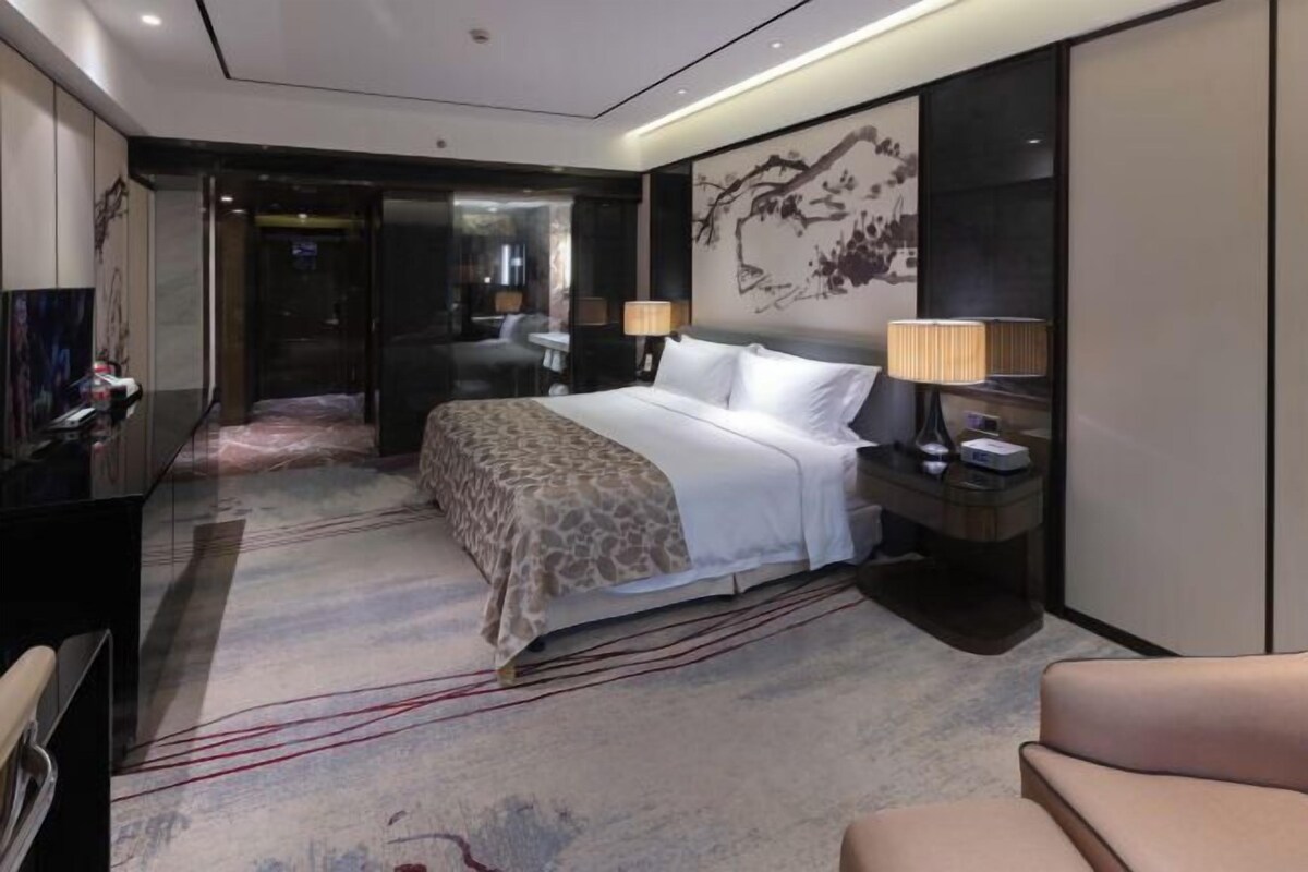 Quarto de hotel moderno com uma cama grande, escrivaninha, televisão e um quadro na parede.