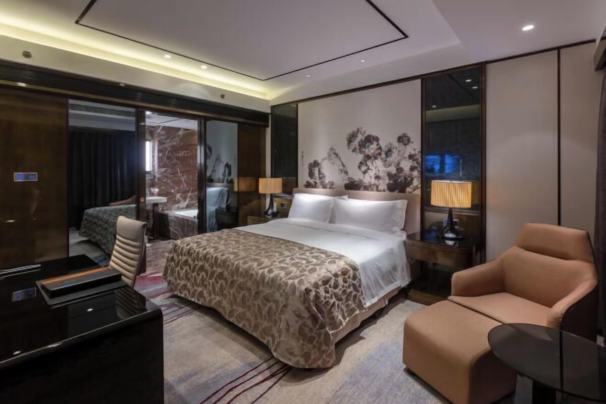 Quarto de hotel moderno com uma cama grande, uma escrivaninha, uma cadeira e um sofá.