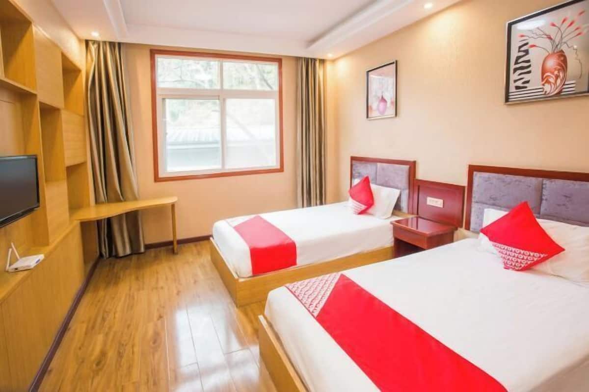 Quarto de hotel com duas camas, televisão, escrivaninha e janela com cortinas.