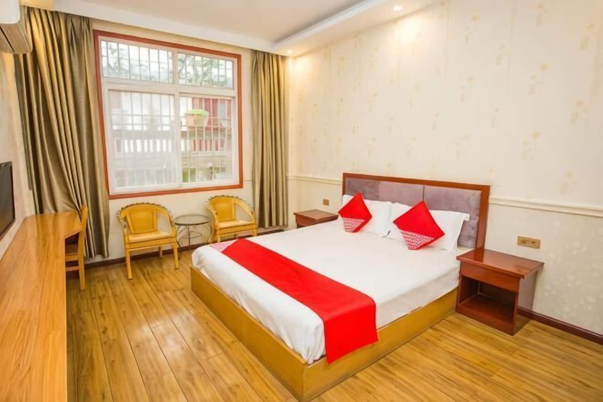Quarto de hotel com uma cama grande, uma mesa de escritório, duas cadeiras, uma pequena mesa e uma janela com cortinas.