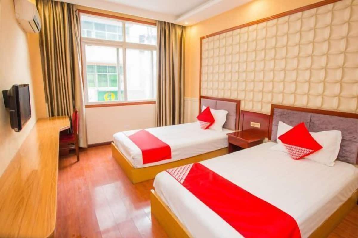 Quarto de hotel com duas camas, televisão, janela com cortinas e chão de madeira.