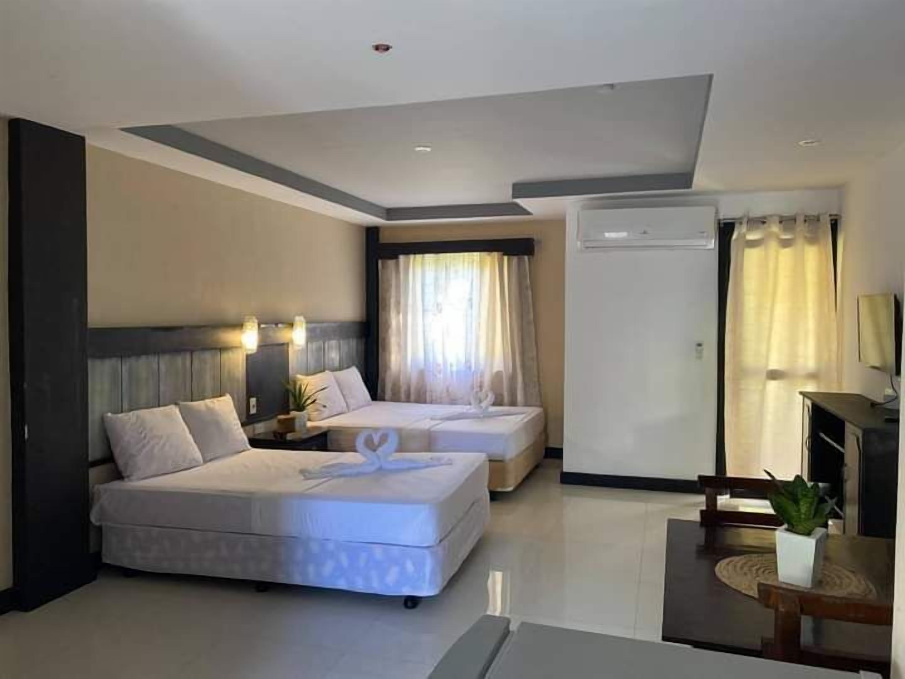 Quarto de hotel moderno com uma cama grande, uma cama menor, uma escrivaninha e uma cadeira.