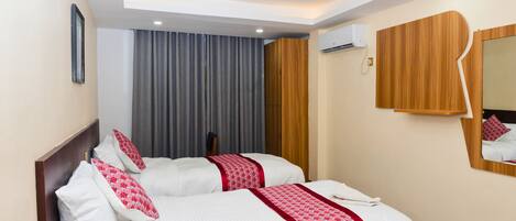 Quarto de hotel com duas camas, uma cabeceira de madeira, um espelho e uma janela com cortinas.