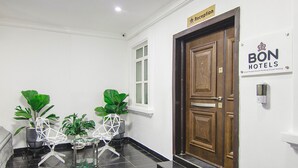 Uma área de recepção com balcão, plantas em vasos e placa indicativa.