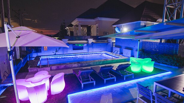Área de piscina externa com espreguiçadeiras, uma mesa e um grande guarda-sol.