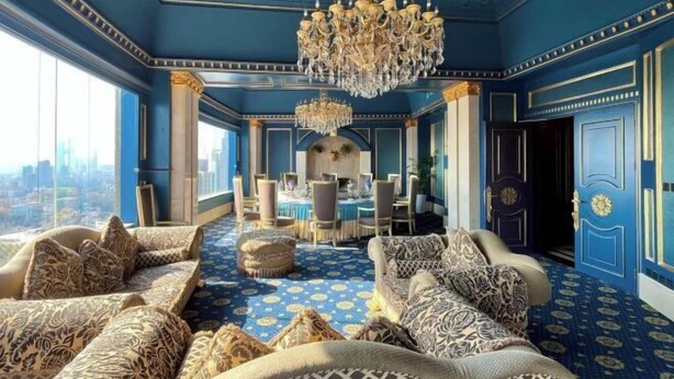 Quarto luxuoso com um grande candelabro, teto ricamente decorado e vista para a cidade.