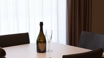 Uma mesa de jantar com uma garrafa de vinho e um copo, em frente a uma janela com cortinas.