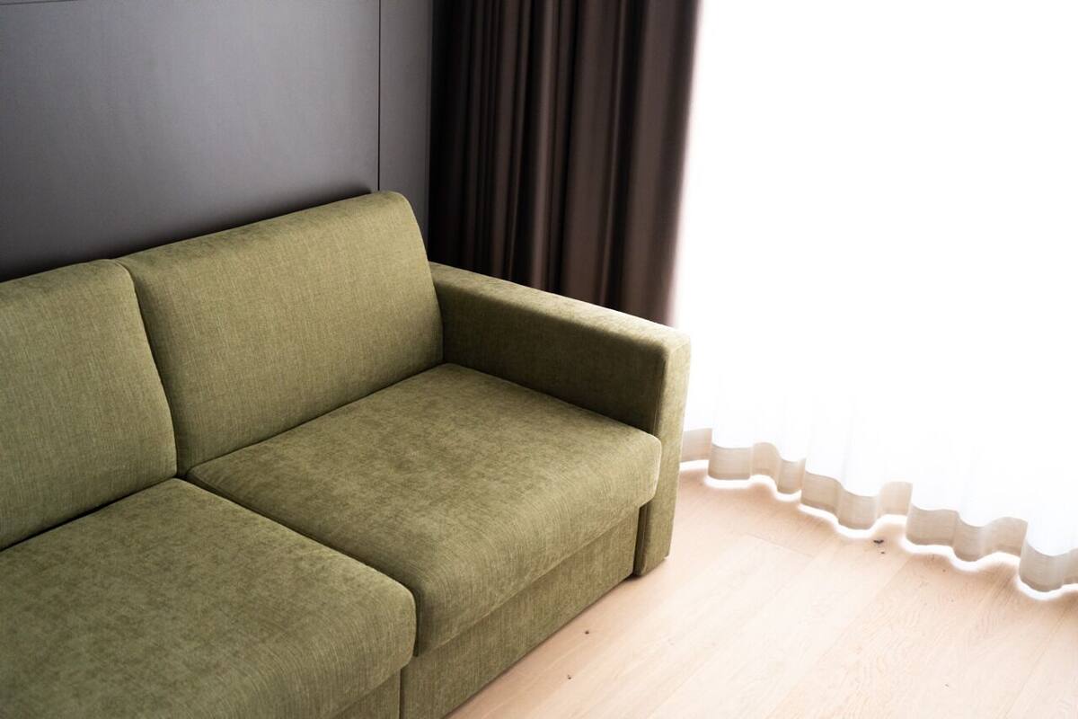 Um sofá verde num quarto com soalho de madeira e parede cinzenta.