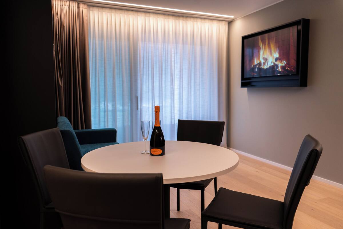 Uma área de jantar moderna com uma mesa redonda, cadeiras pretas e uma garrafa de champanhe.