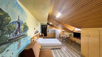 Quarto compacto com cama, pequena escrivaninha, cadeira, painel decorativo e cozinha compacta.