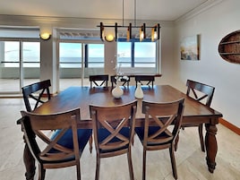 Uma sala de jantar com uma grande mesa de madeira, seis cadeiras e um lustre.