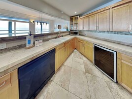 Cozinha moderna com armários de madeira, máquina de lavar louça, micro-ondas e uma janela ampla com vista.