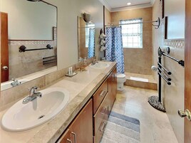 Uma casa de banho moderna com duas pias, sanita, banheira e um separador de chuveiro.