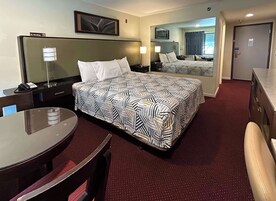 Quarto de hotel com uma cama grande, uma escrivaninha, uma cadeira, um espelho e uma porta.