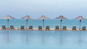 Área à beira da piscina com espreguiçadeiras e guarda-sóis, com vista para o mar.