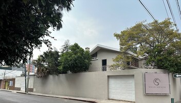 Um edifício moderno com porta de garagem, cercado por árvores e um muro de concreto.