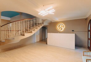 Uma área de recepção moderna com uma escadaria curva, um balcão de atendimento e um logotipo iluminado e distinto na parede.