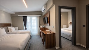 Quarto de hotel com duas camas, uma escrivaninha, uma televisão e uma janela grande.