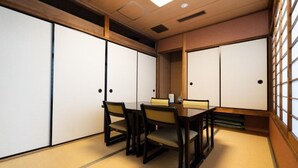 Quarto japonês tradicional com tatames, uma mesa baixa com cadeiras, portas deslizantes e vista através de um shoji.