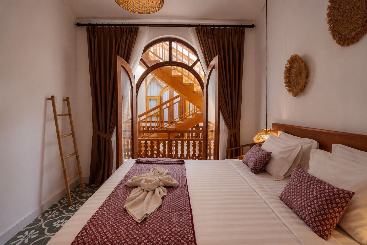 Quarto de hotel com uma cama, uma escada de madeira, vista para um lance de escadas e um tapete estampado.