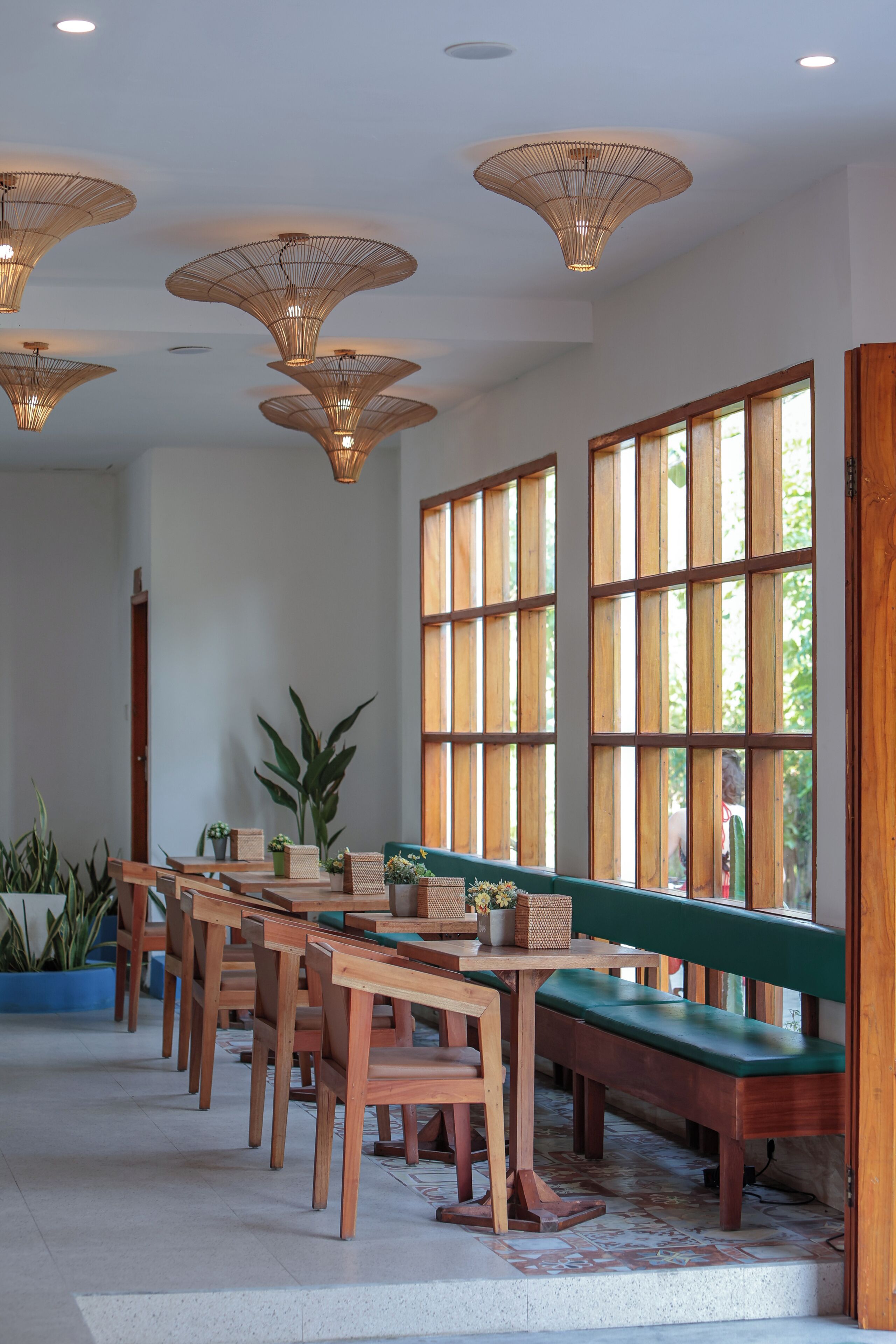 Um espaço interno amplo, com móveis de madeira, grandes janelas e luminárias pendentes.