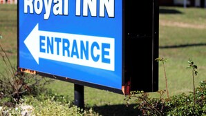 Um sinal azul com texto branco indicando 'Royal INN ENTRANCE' e uma seta apontando para a esquerda.