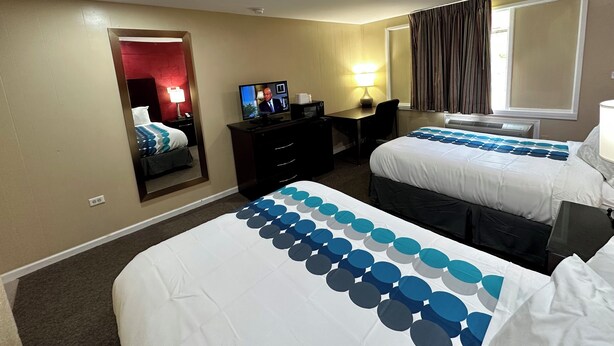 Quarto de hotel com duas camas, uma escrivaninha, uma televisão e um espelho.