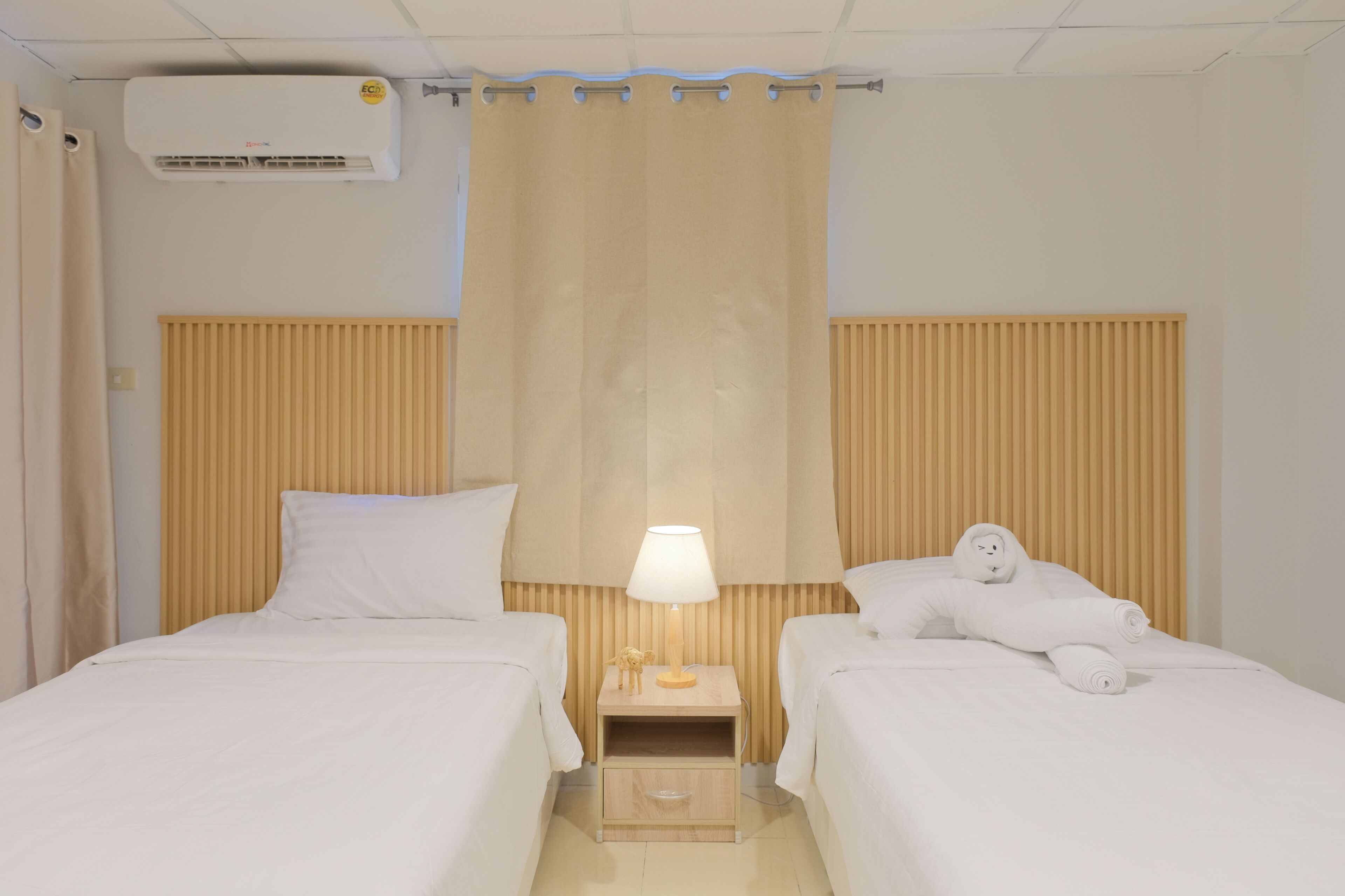 Quarto de hotel com duas camas, uma mesa de cabeceira com abajur e cabeceira de madeira.