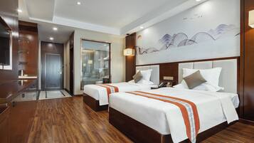 Quarto de hotel com duas camas, piso de madeira, uma pintura grande na parede e um banheiro visível através de uma porta de vidro.