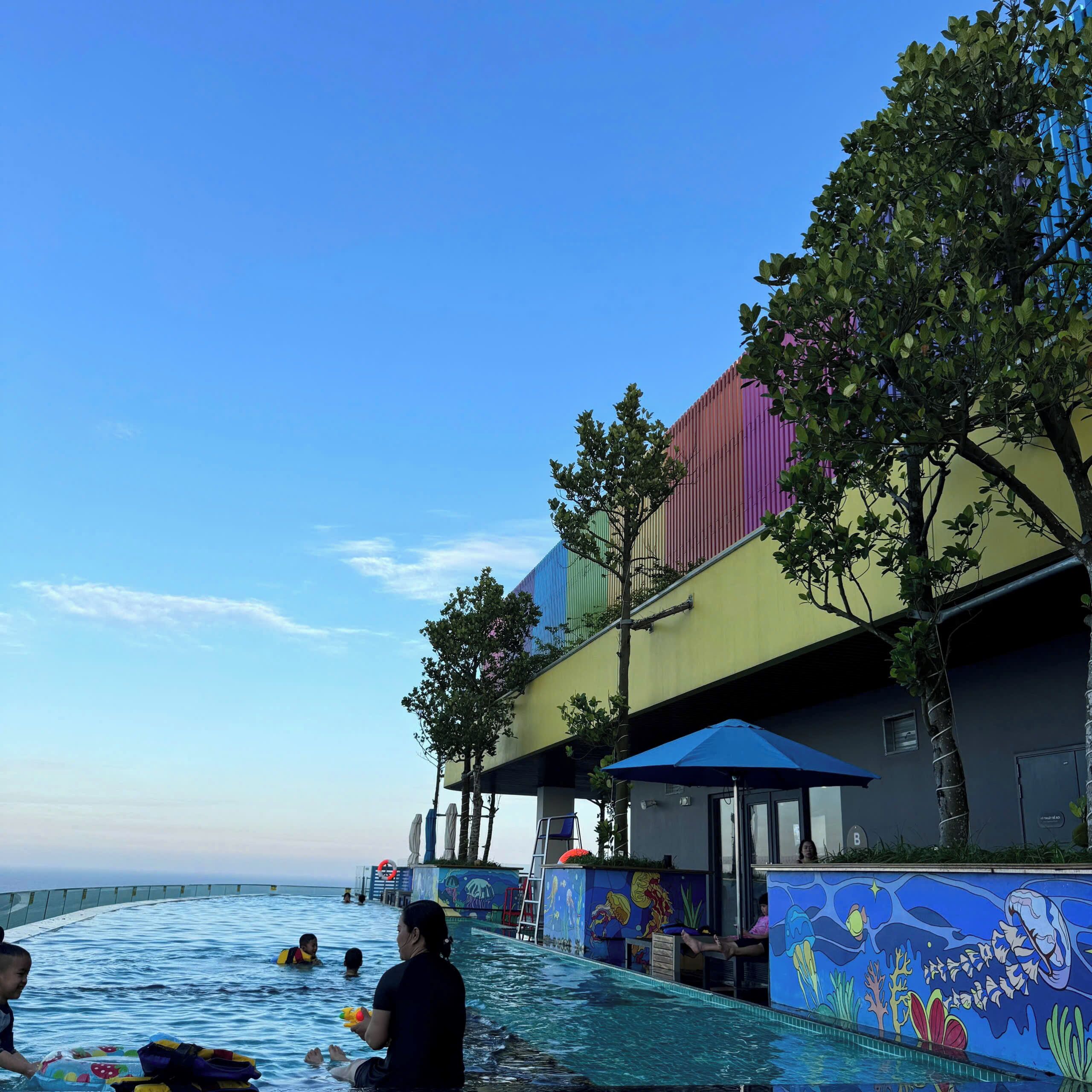 Piscina com um mural, área de estar coberta e um edifício com elementos verticais coloridos.