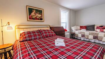 Quarto com uma cama grande, uma cama menor, uma mesa de cabeceira, um abajur e um quadro na parede.