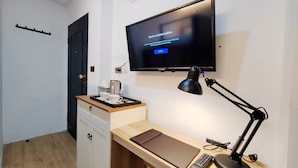 Quarto de hotel com escrivaninha, televisão exibindo mensagem de autorização de dispositivo, luminária de mesa, controle remoto e cafeteira.