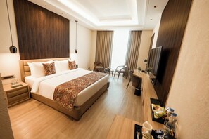 Quarto de hotel moderno com uma cama grande, uma mesa de escritório, uma cadeira e uma televisão.