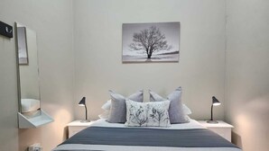Um quarto com uma cama, duas mesas de cabeceira, um abajur, um espelho fixado na parede e um quadro com uma imagem de uma árvore.