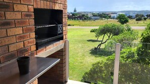 Área de churrasco ao ar livre construída em tijolos, com vista para um campo gramado e árvores.