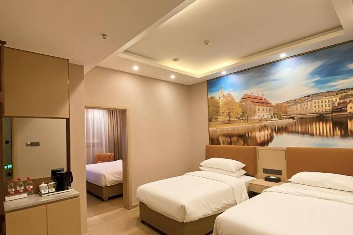 Quarto de hotel com duas camas, um espelho grande, um minibar e um mural com uma vista urbana.